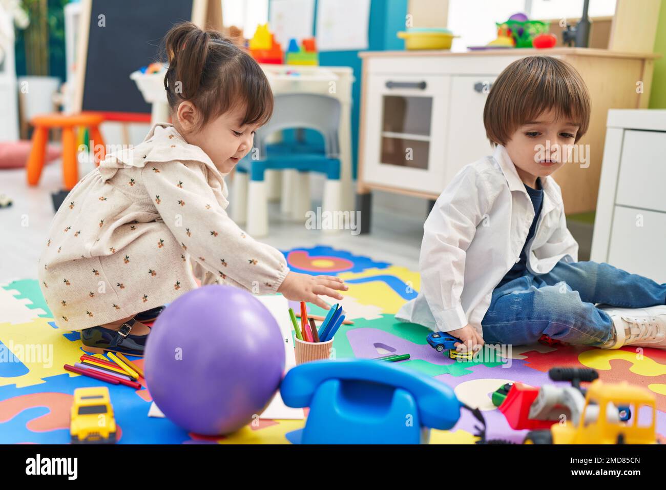 Two kids playing with toys sitting on floor at kindergarten Stock Photo ...