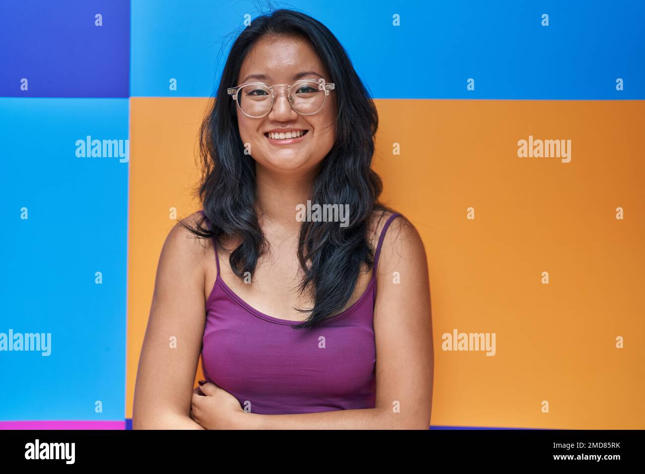 Asian young woman standing over colorful background looking positive ...