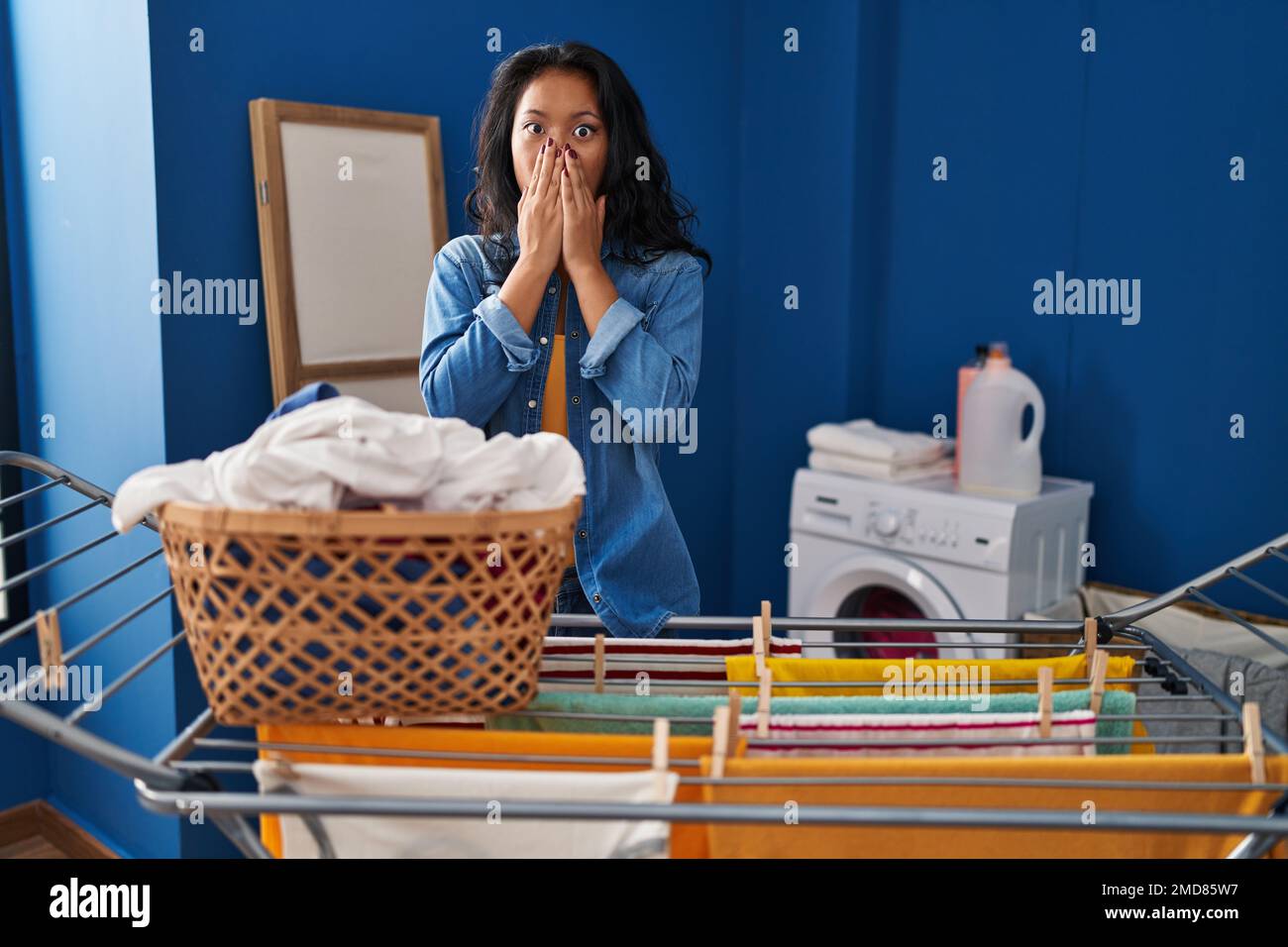 Young asian woman hanging clothes at clothesline shocked covering mouth ...