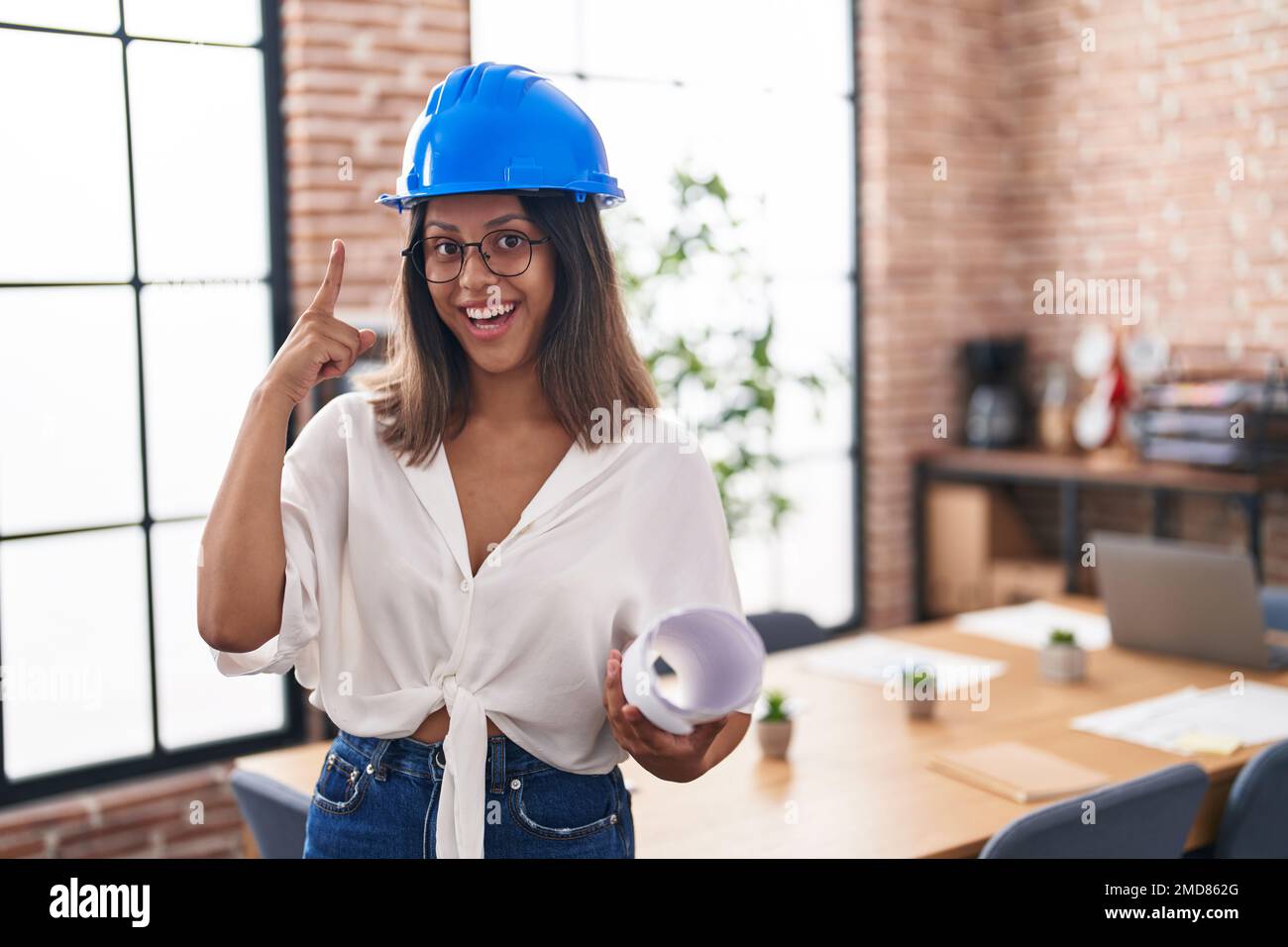 Hispanic young woman wearing architect hardhat at office smiling happy ...