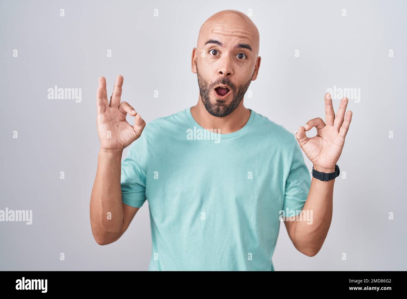 Middle age bald man standing over white background looking surprised ...