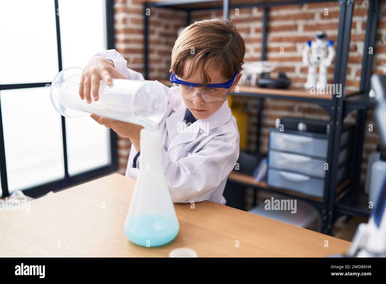 Adorable hispanic boy student pouring liquid on test tube at laboratory ...