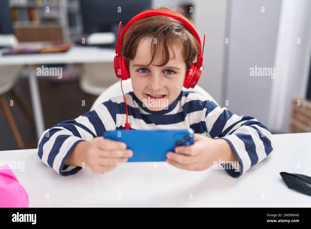 Adorable hispanic boy student using smartphone and headphones at ...