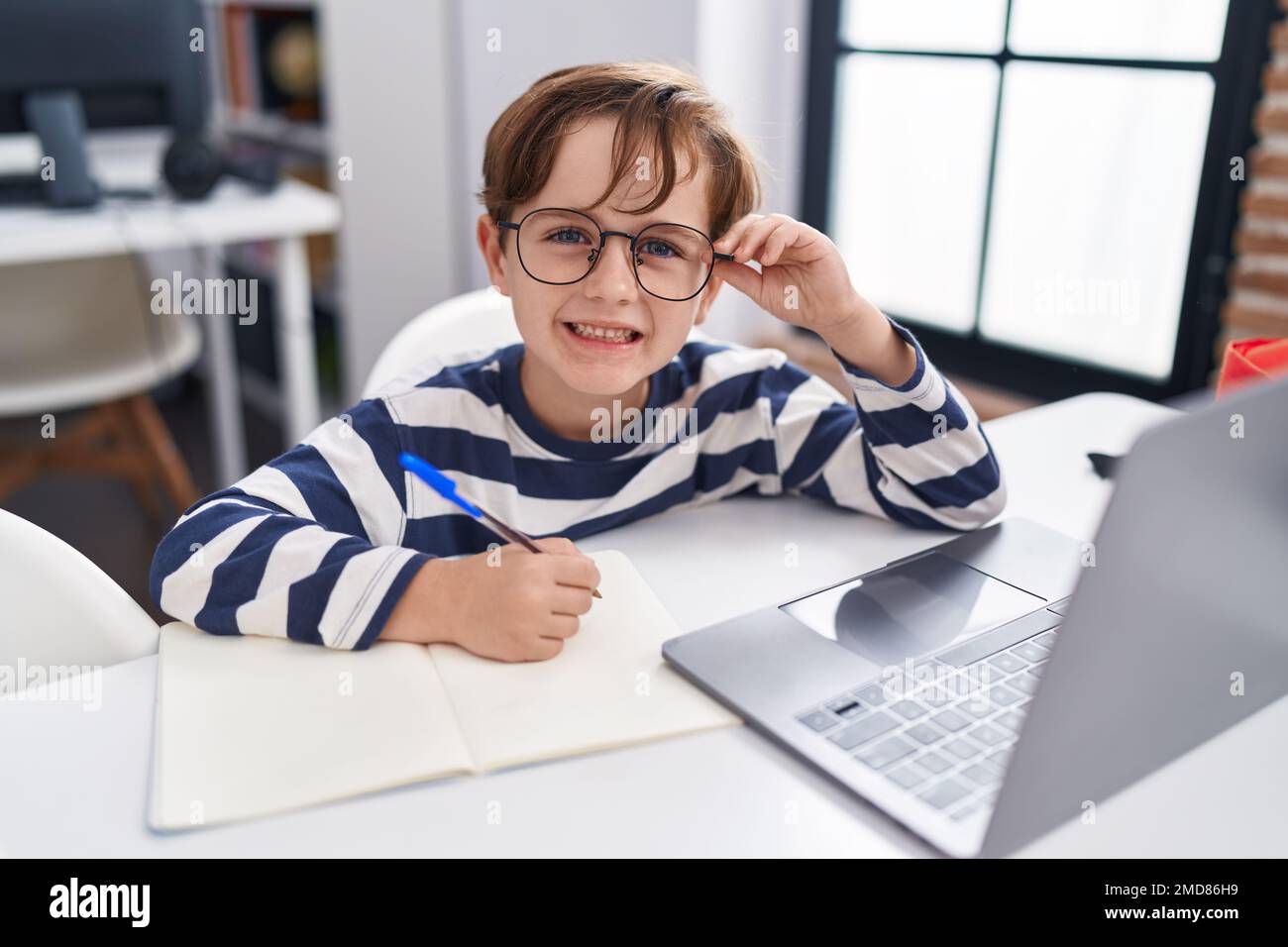 Adorable hispanic boy student using computer writing on notebook at ...