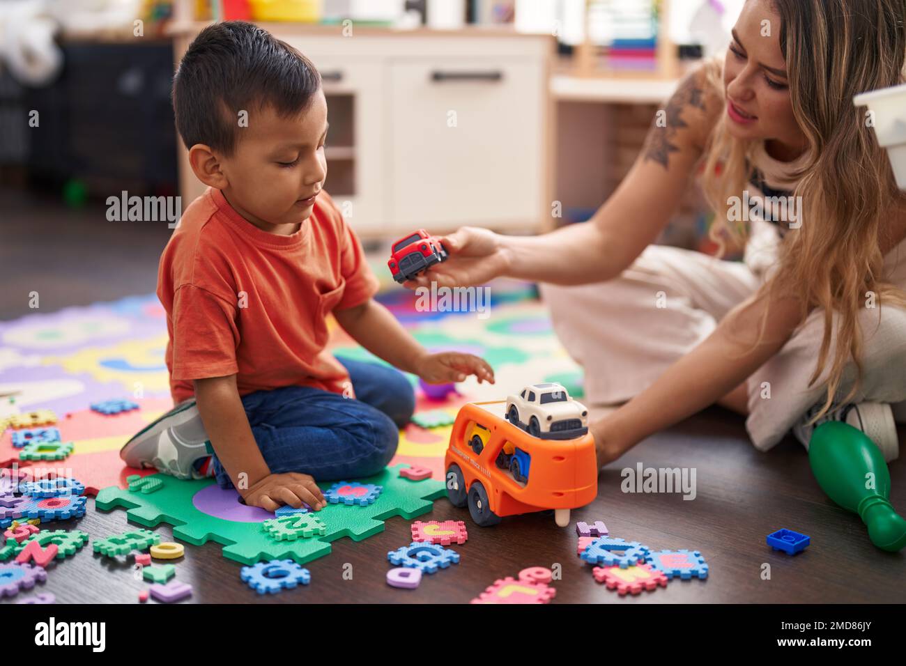 Teacher and toddler playing with cars toy sitting on floor at ...