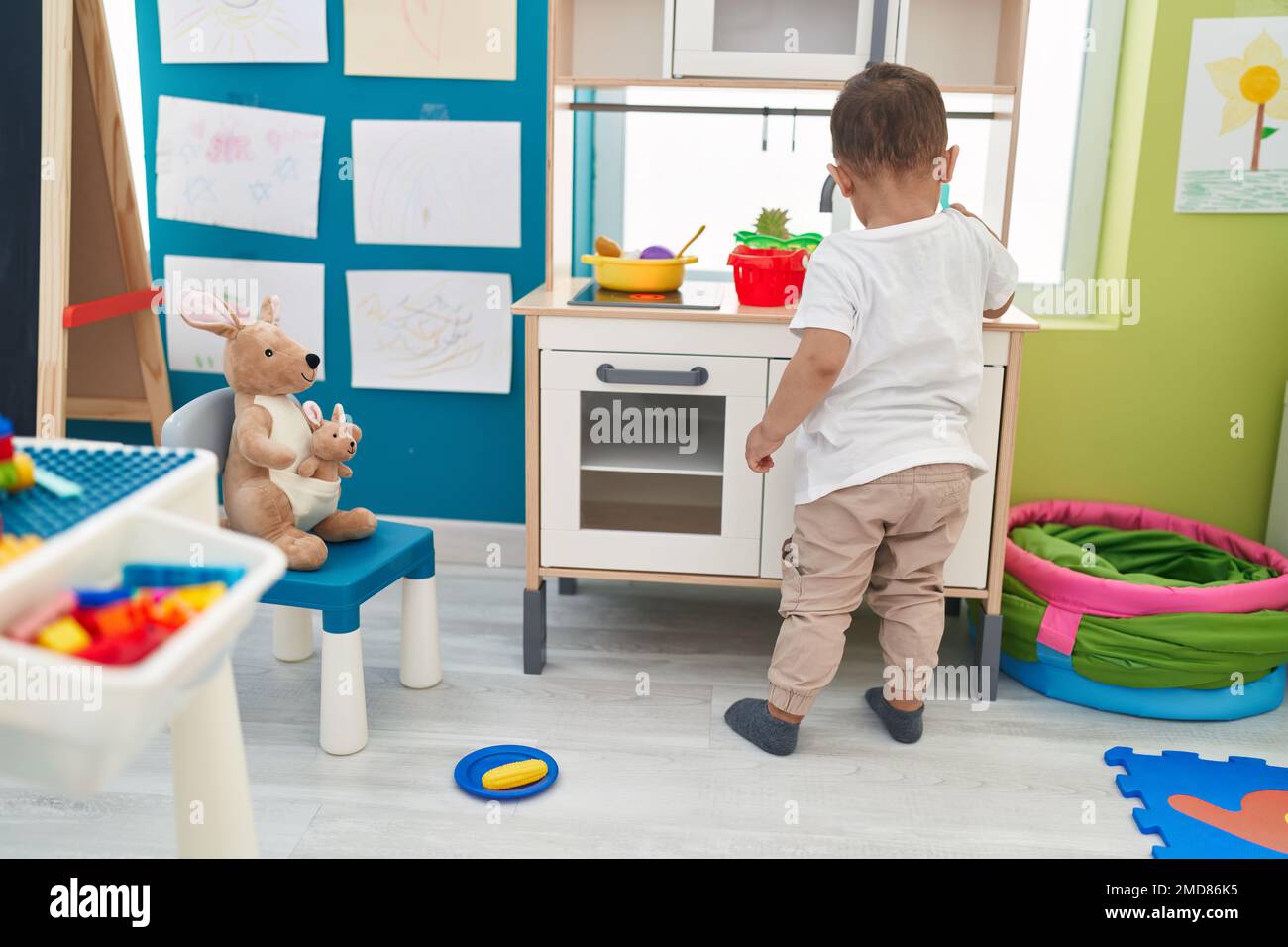 Adorable hispanic toddler playing with play kitchen standing at ...