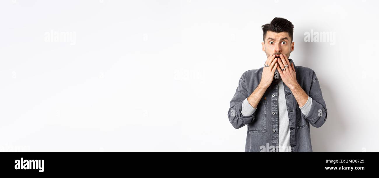 Shocked caucasian guy gasping alarmed, cover mouth with hands and ...