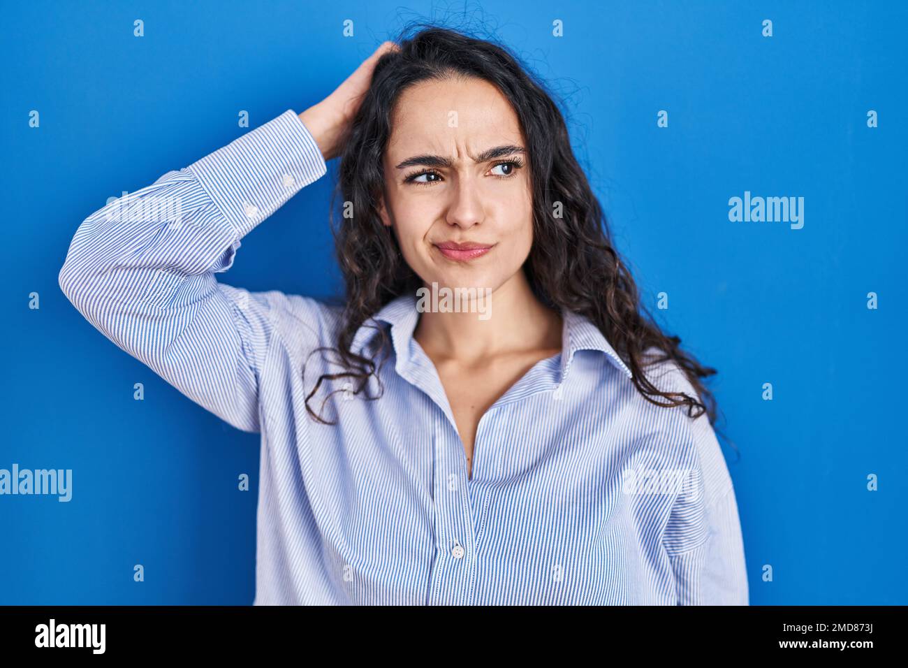 Young brunette woman standing over blue background confuse and wonder ...