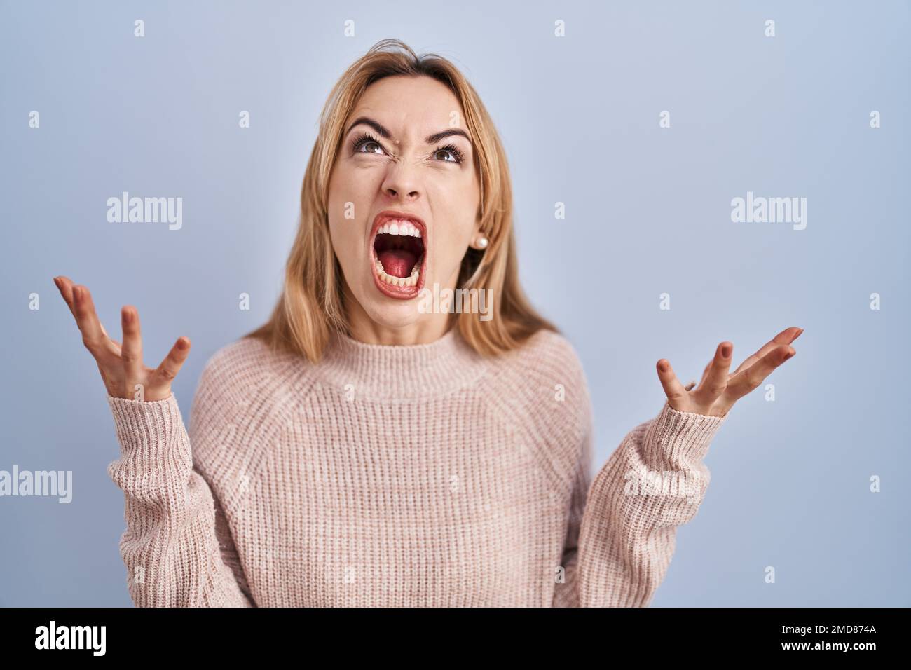 Hispanic woman standing over blue background crazy and mad shouting and ...