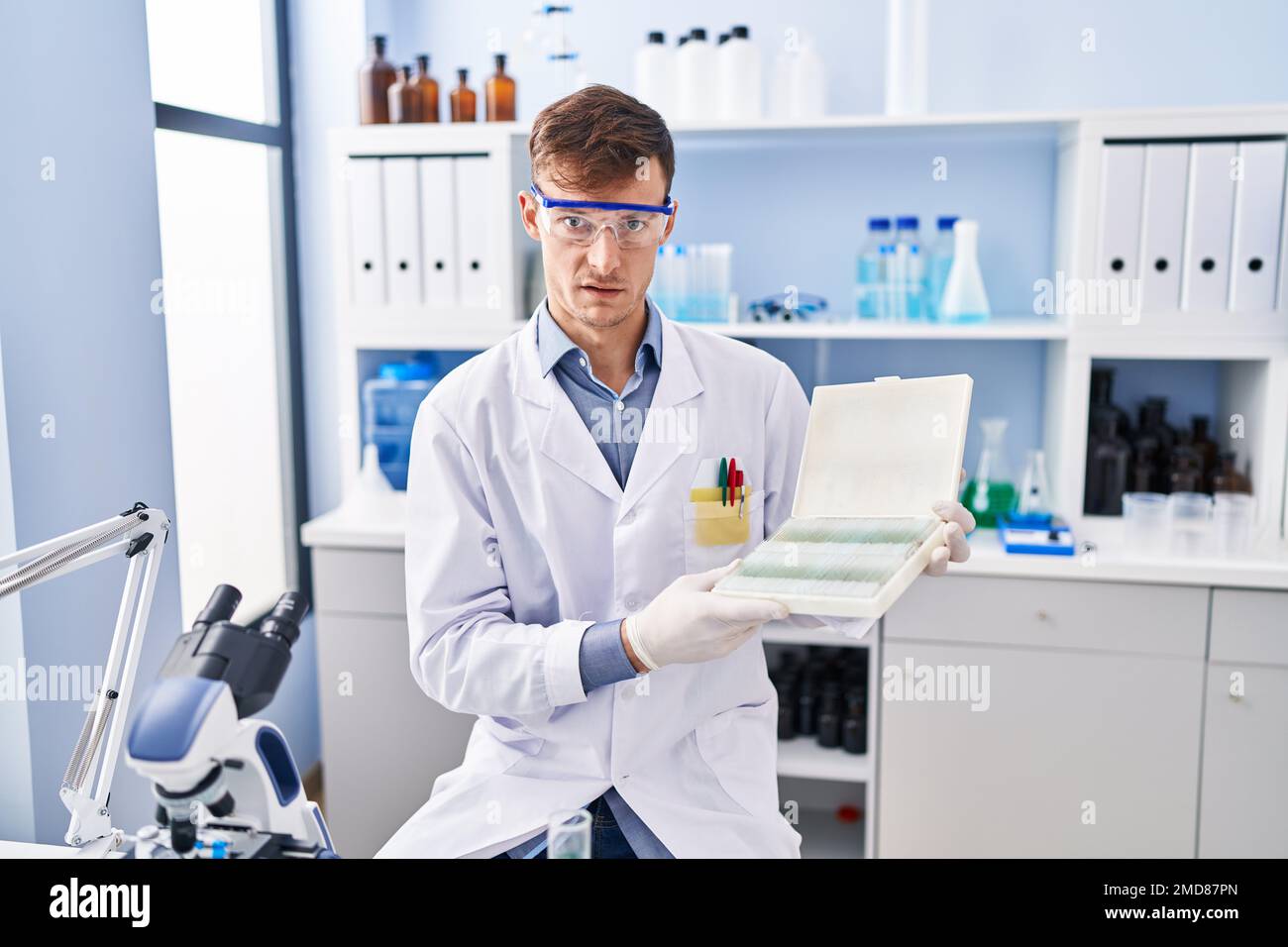 Caucasian man working at scientist laboratory in shock face, looking ...