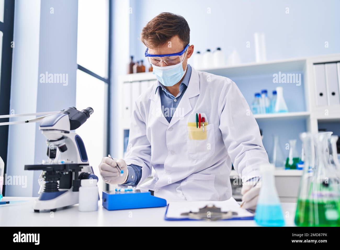 Young man scientist wearing medical mask weighing pills at laboratory ...