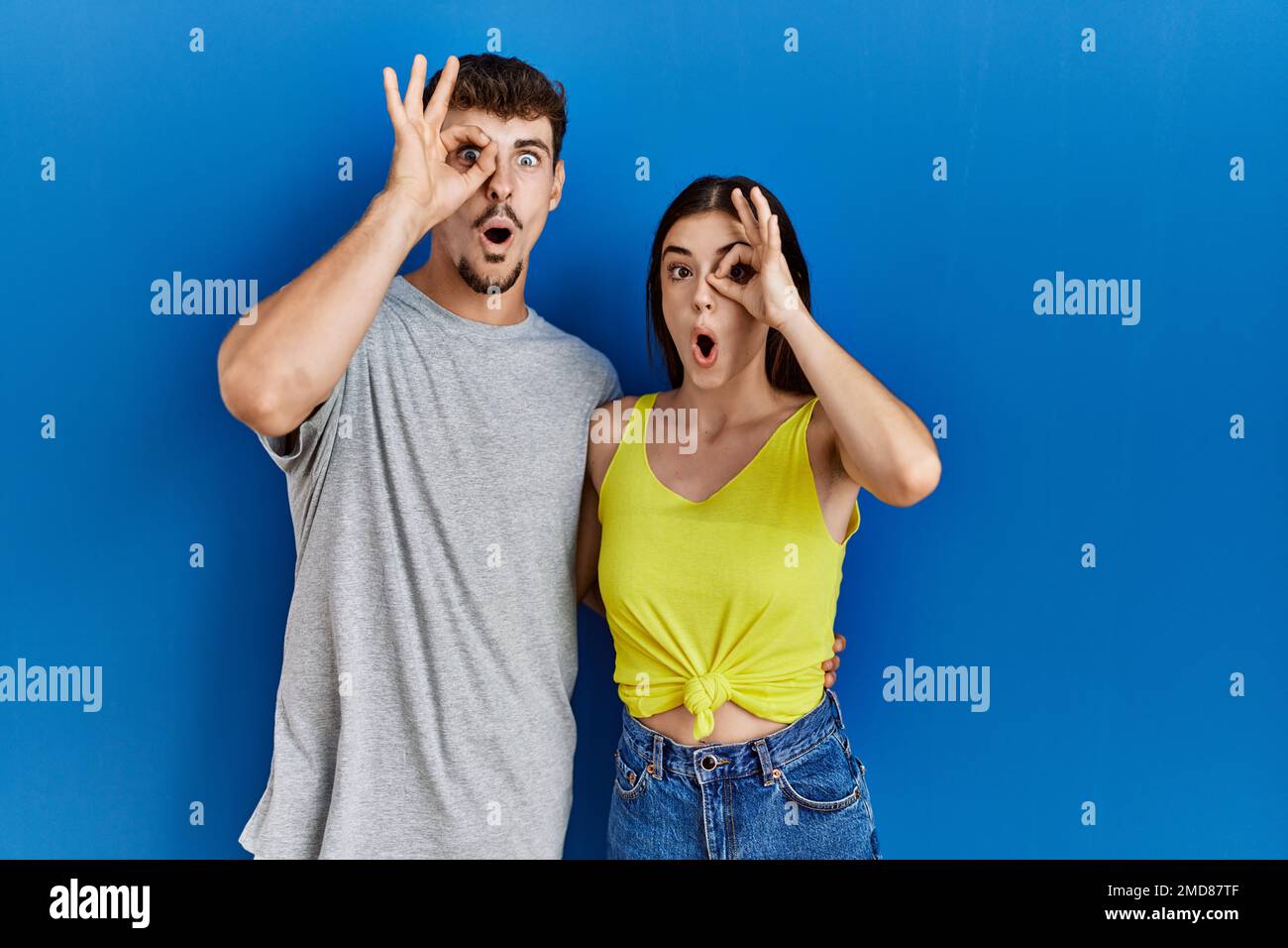 Young hispanic couple standing together over blue background doing ok ...