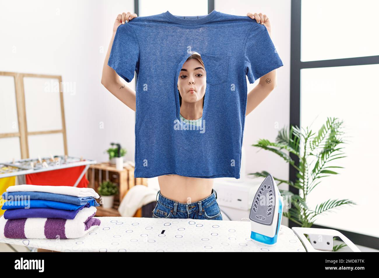 Young hispanic woman ironing holding burned iron shirt at laundry room ...