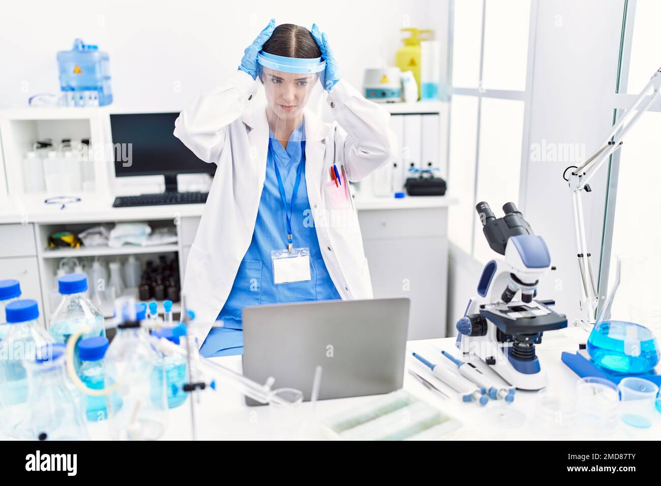 Young hispanic woman wearing scientist uniform suffering from headache ...