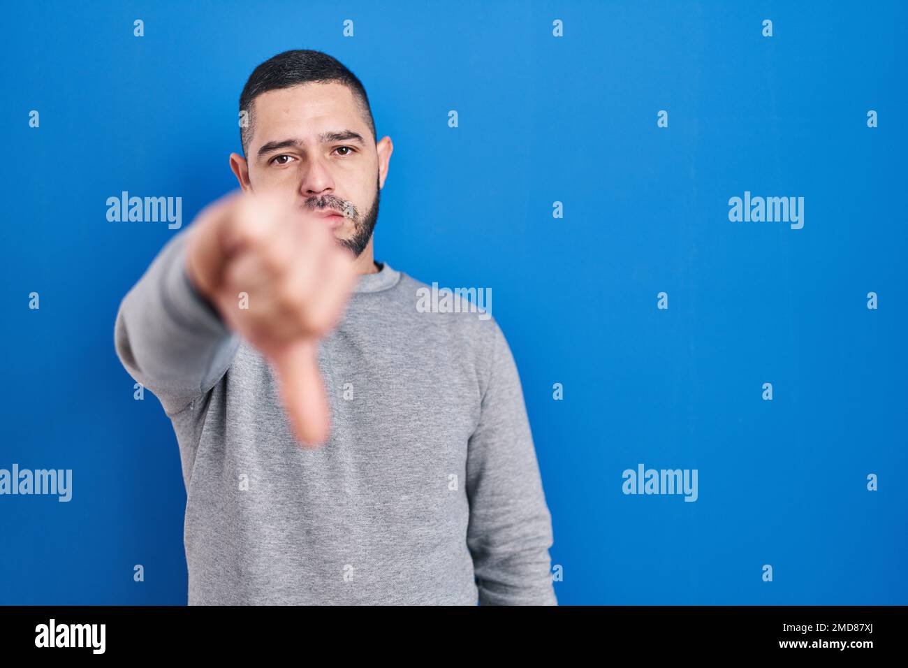 Hispanic man standing over blue background looking unhappy and angry ...