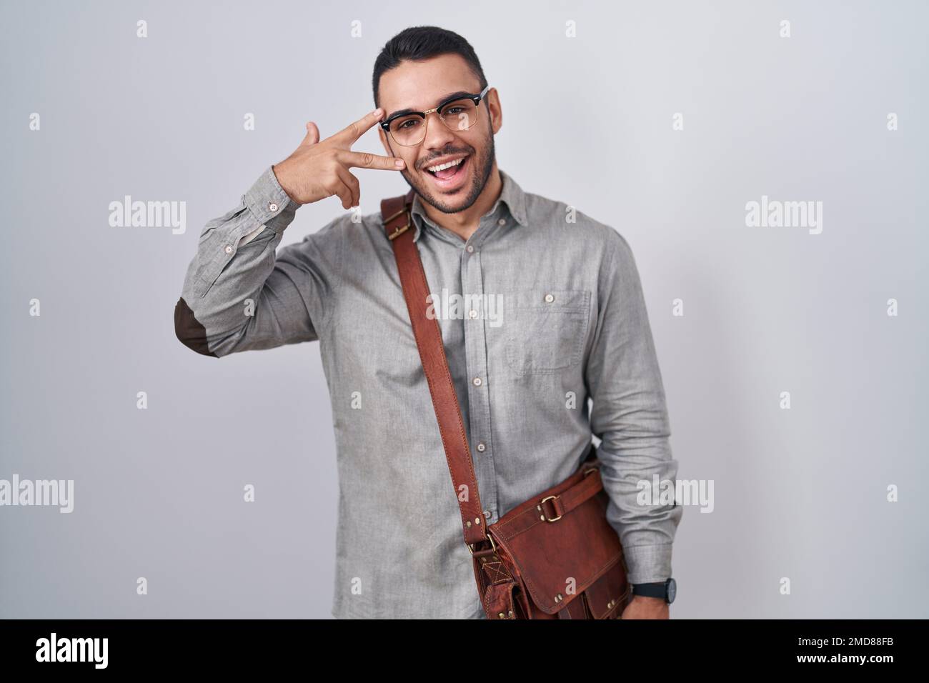 Young hispanic man wearing suitcase doing peace symbol with fingers ...