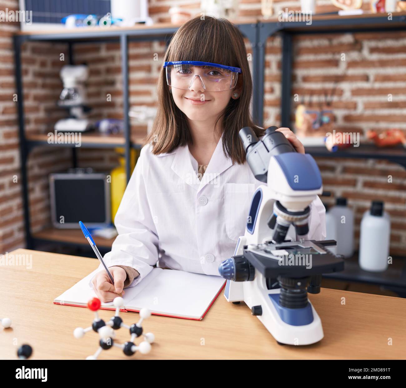 Adorable hispanic girl student using microscope writing on noteboo at ...