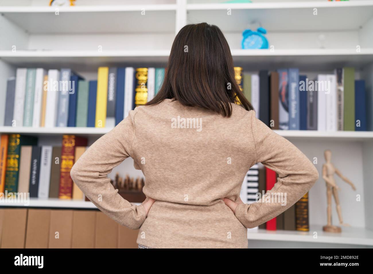 Adorable hispanic girl student looking books of shelving at library ...