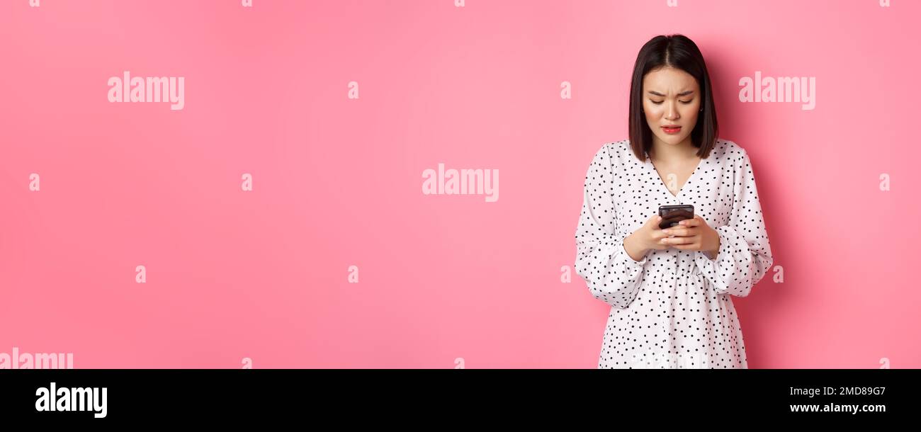 Nervous and concerned asian woman reading message on smartphone ...