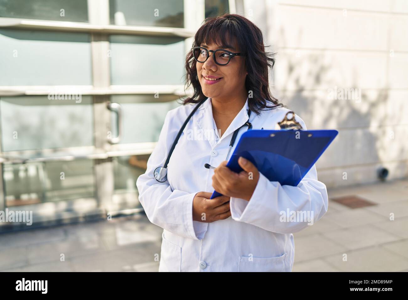 Young beautiful latin woman doctor smiling confident holding clipboard ...