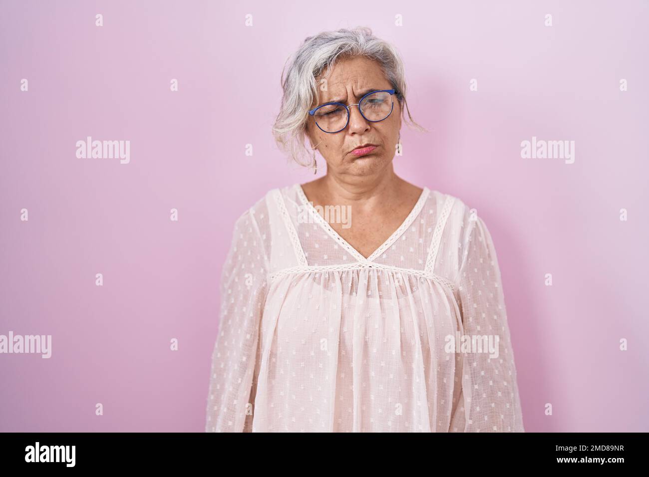 Middle age woman with grey hair standing over pink background depressed ...