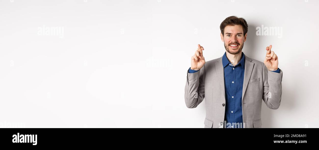 Hopeful smiling businessman looking optimistic, cross fingers good luck ...