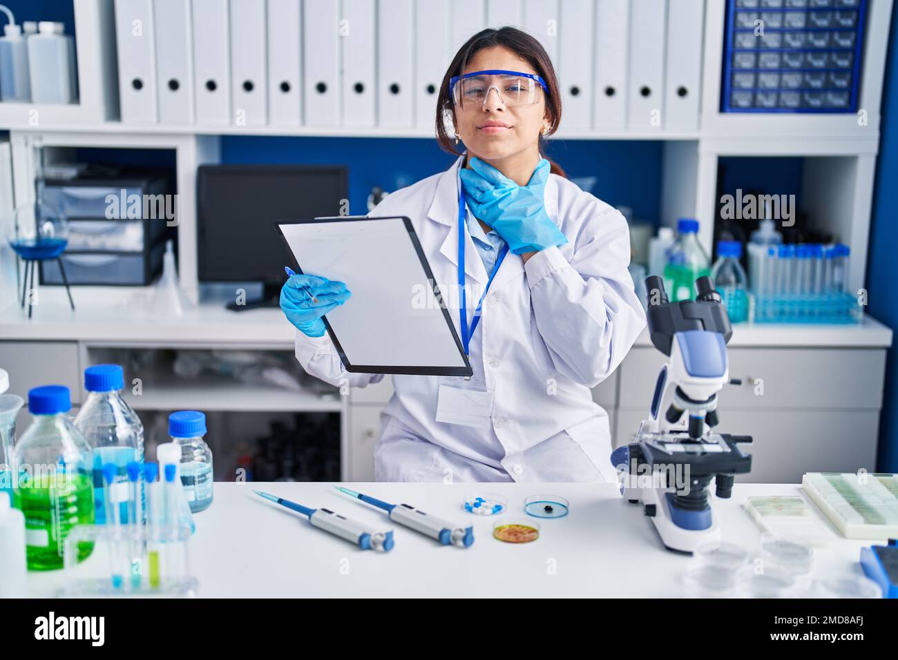 Hispanic young woman working at scientist laboratory touching painful ...
