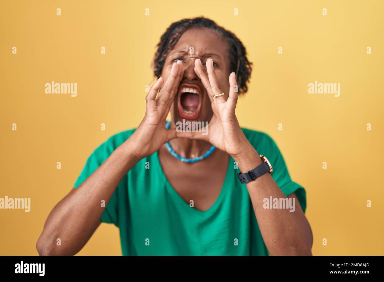 African woman with dreadlocks standing over yellow background shouting ...