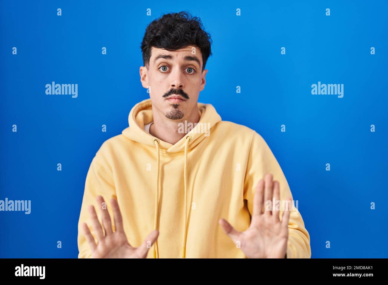 Hispanic man standing over blue background moving away hands palms ...