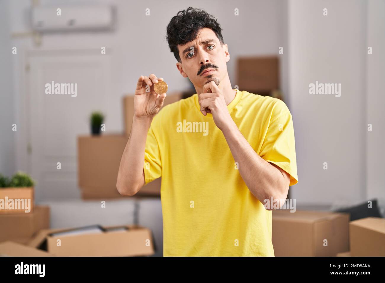 Hispanic man holding bitcoin at new home skeptic and nervous, frowning ...