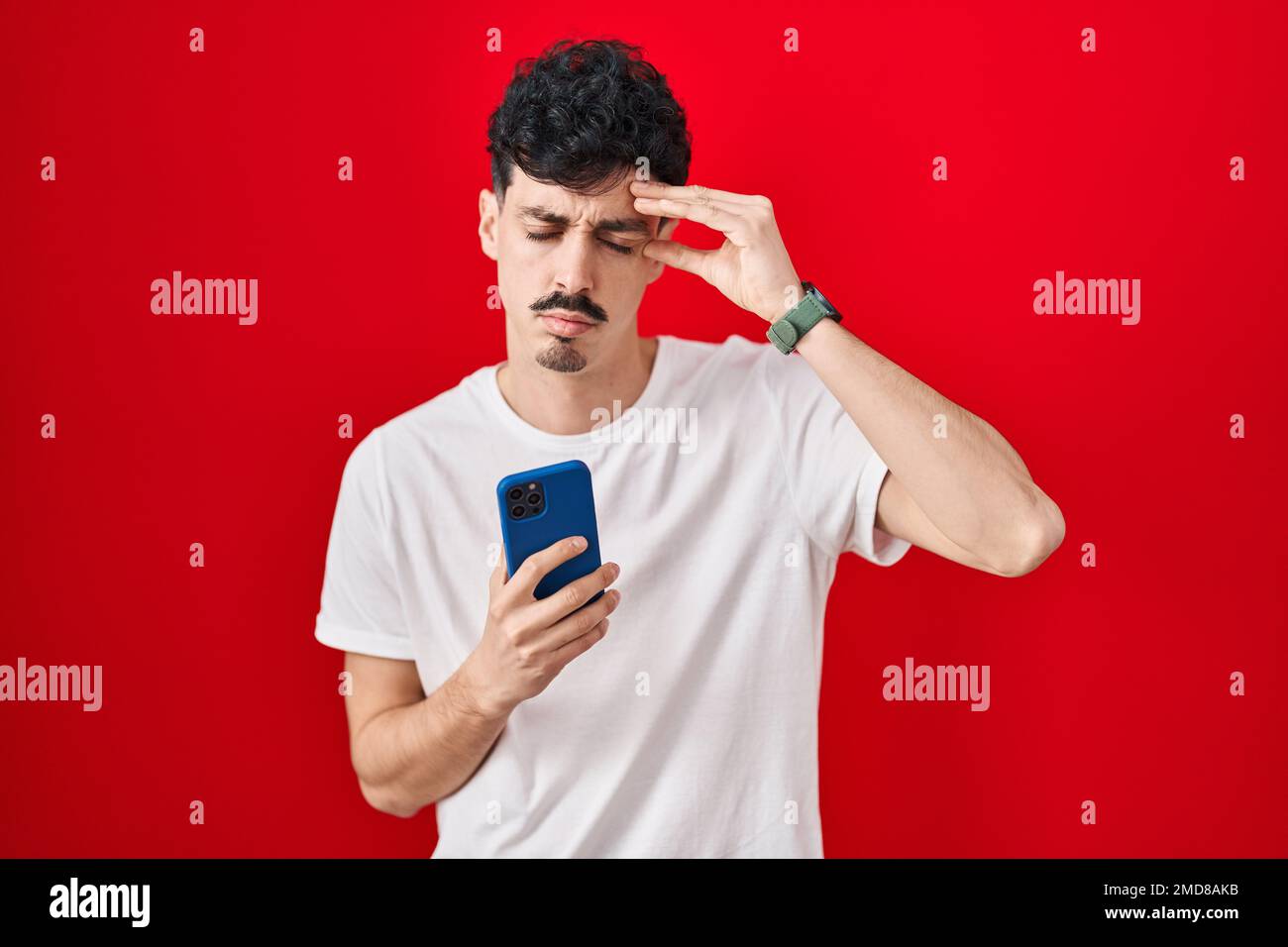 Hispanic man using smartphone over red background worried and stressed ...