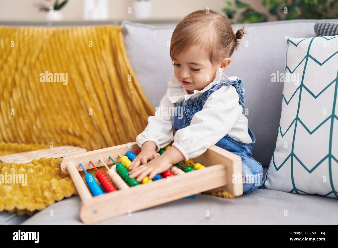 Adorable blonde toddler playing with abacus sitting on sofa at home ...