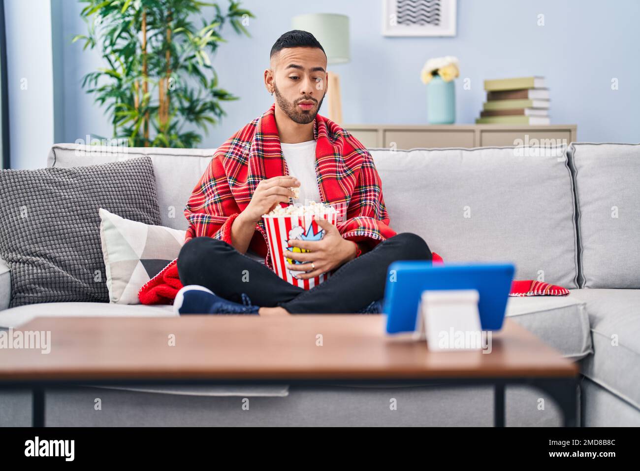 Young hispanic man eating popcorn watching movie on tablet device ...