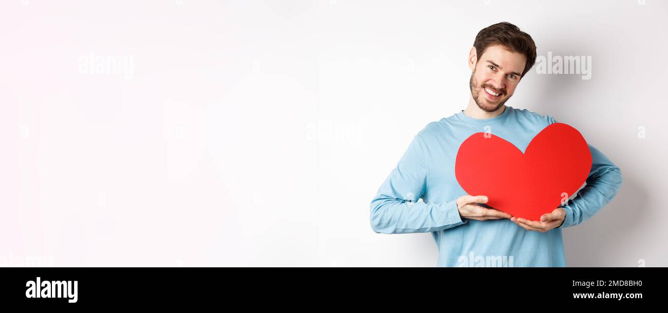 Charming lover man holding Valentines day red heart and smiling, I love ...