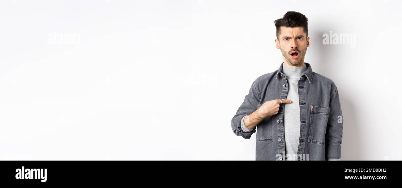 Offended young man being accused, frowning and pointing at himself ...