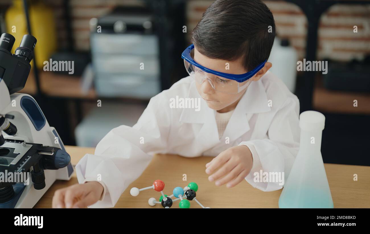 Adorable hispanic boy student holding molecules toy at laboratory ...