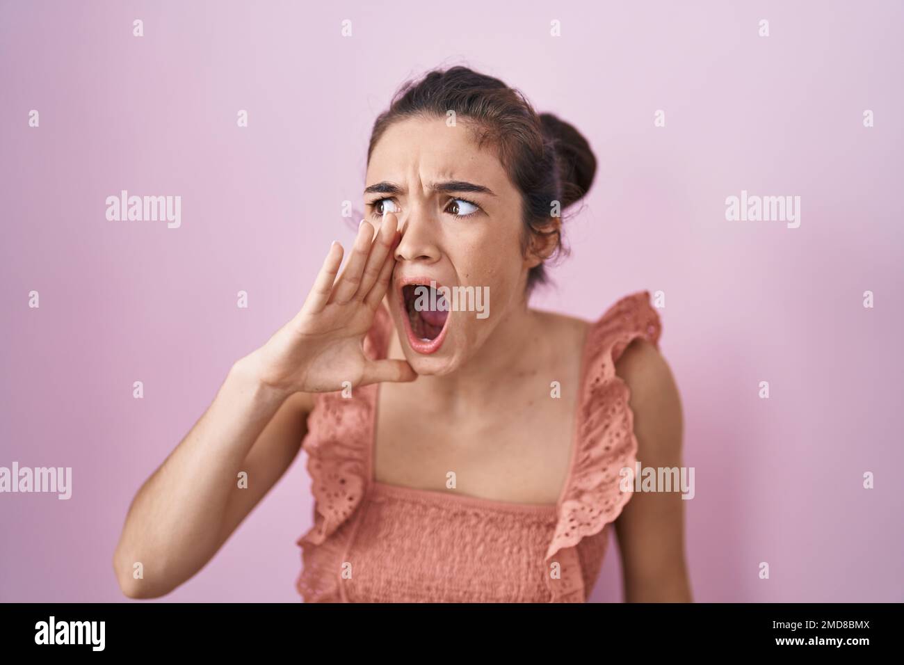 Young teenager girl standing over pink background shouting and ...