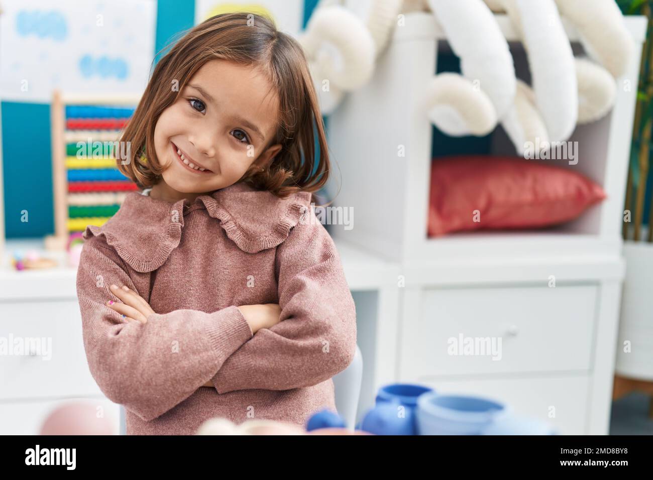 Adorable hispanic girl smiling confident sitting on table with arms crossed gesture at ...