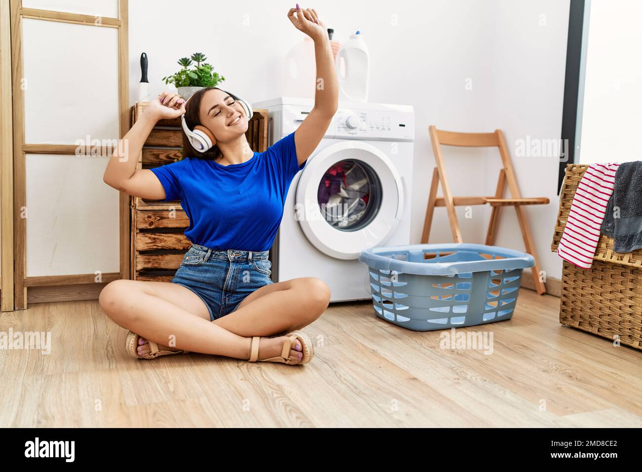 Young caucasian woman listening to music waiting for washing machine at ...