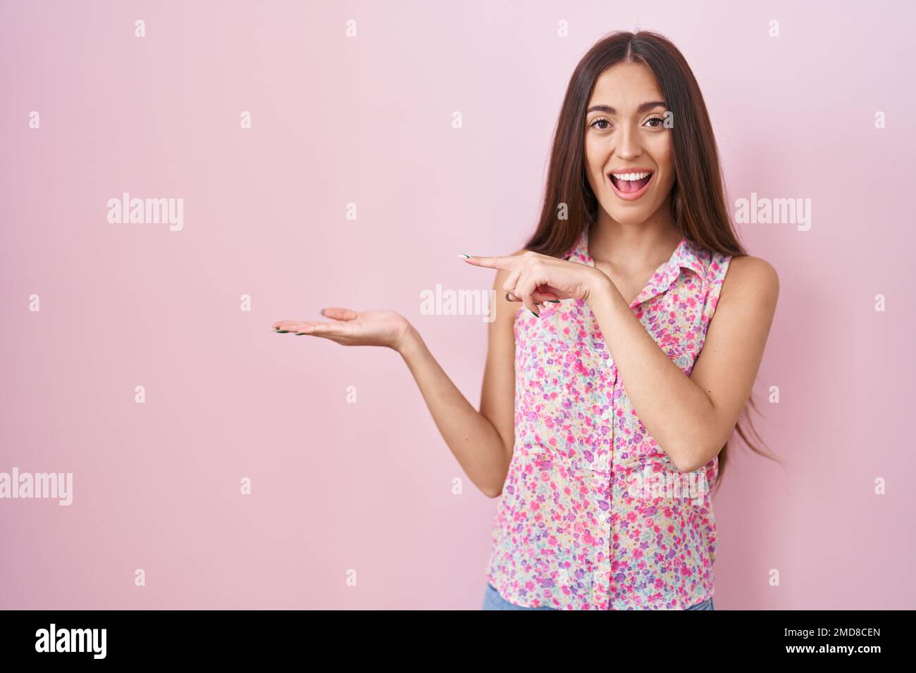 Young hispanic woman with long hair standing over pink background ...