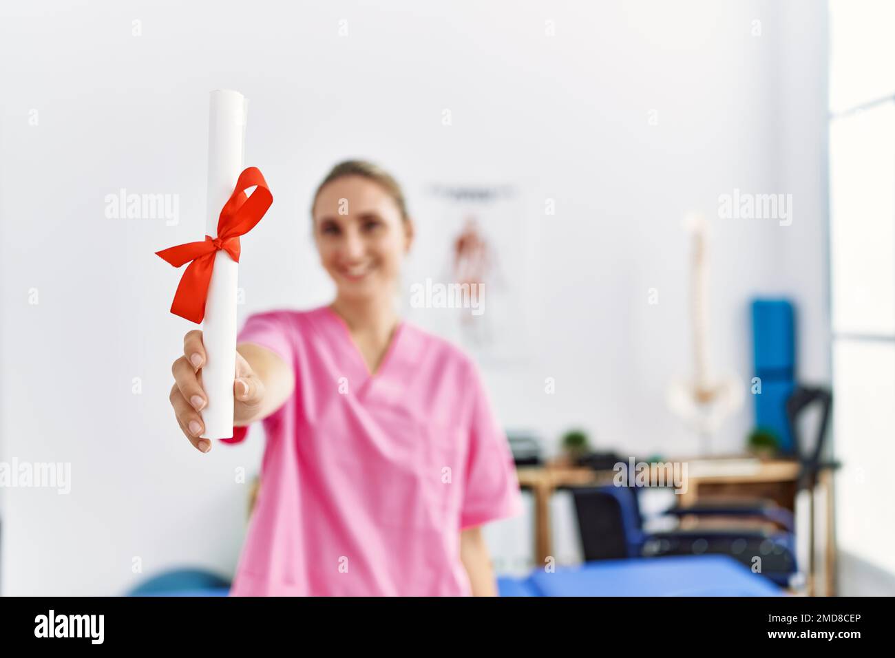 Young blonde woman wearing physiotherapist uniform holding diploma at ...