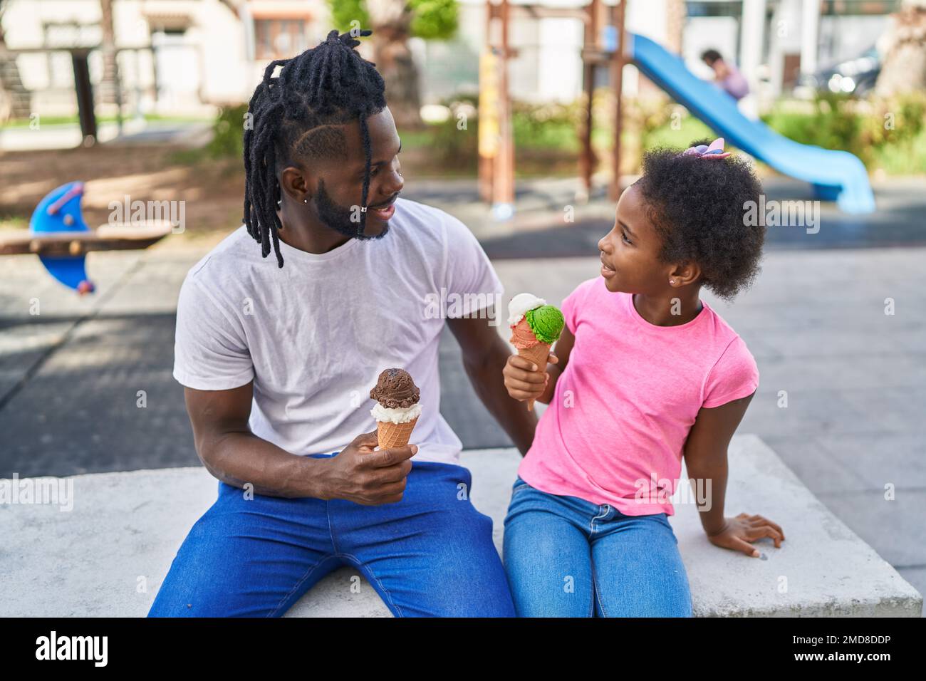 Father and daughter eating ice cream sitting together on bench at park ...