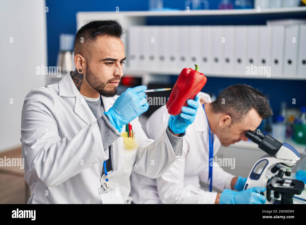 Two men scientist injecting liquid on red pepper using microscope at ...