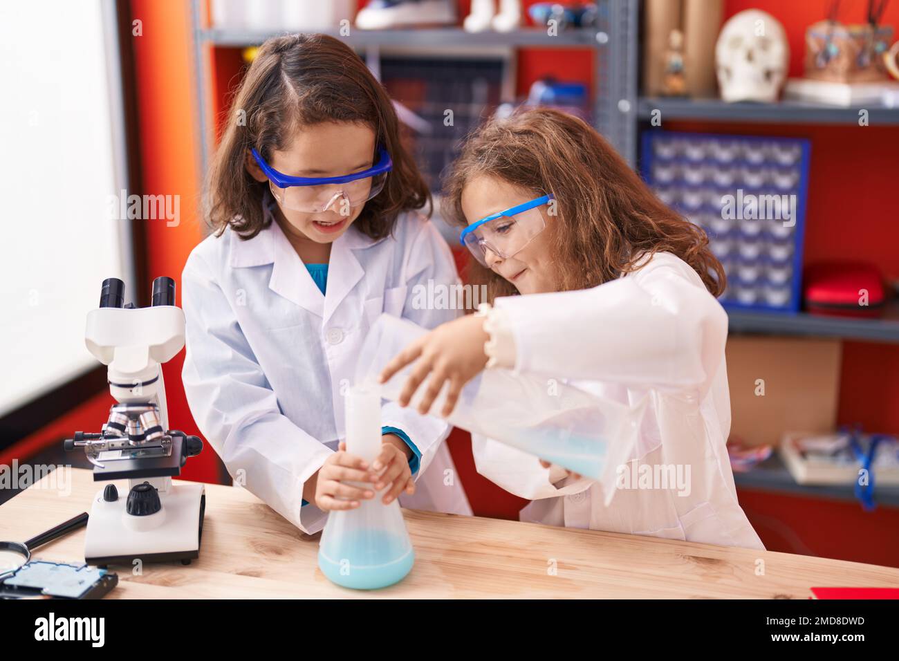 Two kids students pouring liquid on test tube at laboratory classroom ...