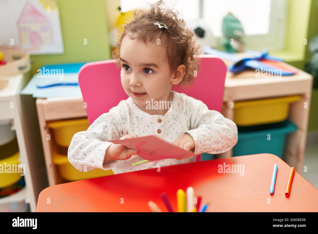 Adorable hispanic toddler student smiling confident cutting paper at ...