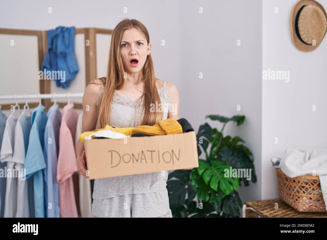 Young caucasian woman holding donations box for charity in shock face ...