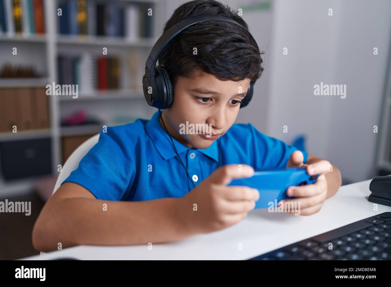 Adorable hispanic boy student using smartphone and headphones at ...