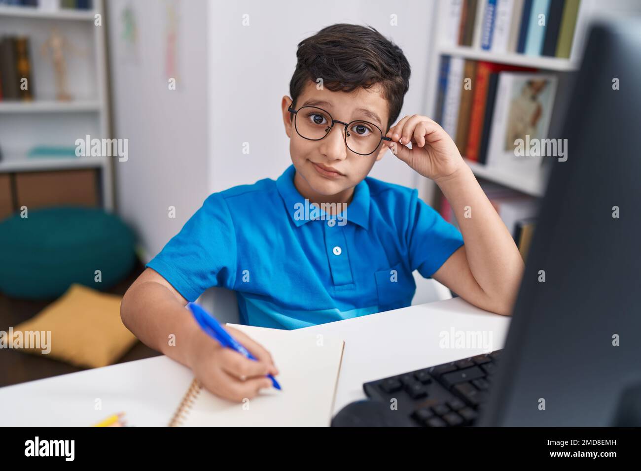 Adorable hispanic boy student using computer writing on notebook at ...