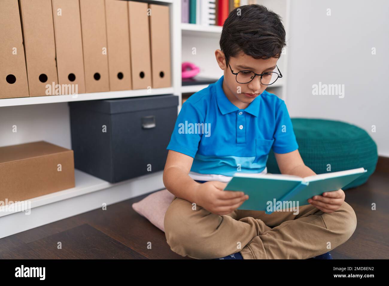 Adorable hispanic boy student reading book at library school Stock ...