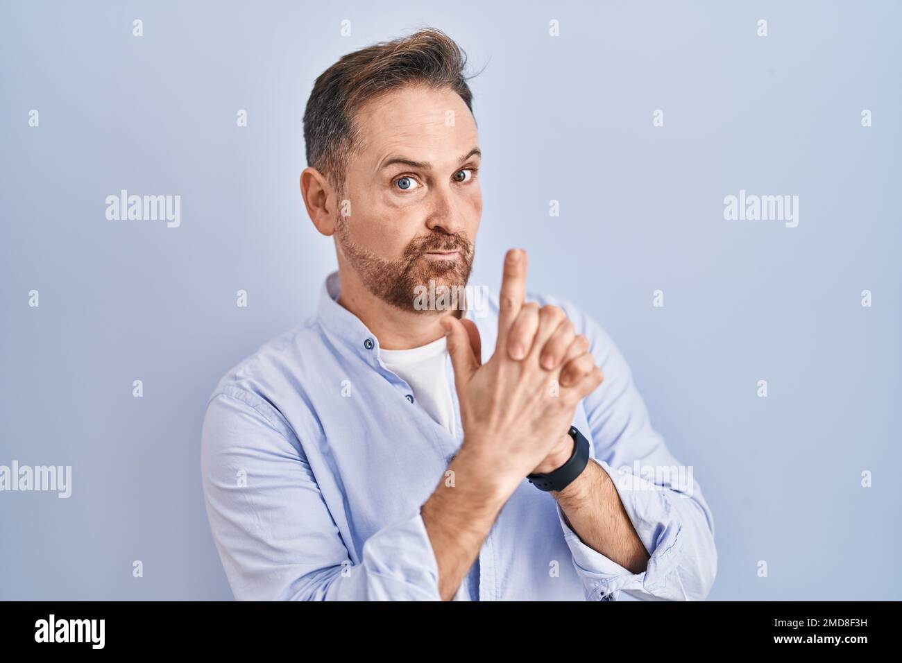 Middle age caucasian man standing over blue background holding symbolic ...